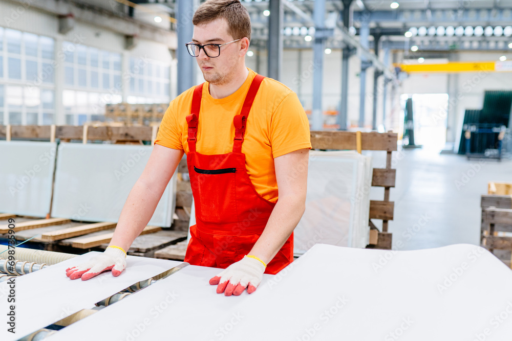 Conveyor production of large sheets of cut glass. Male worker removes ...