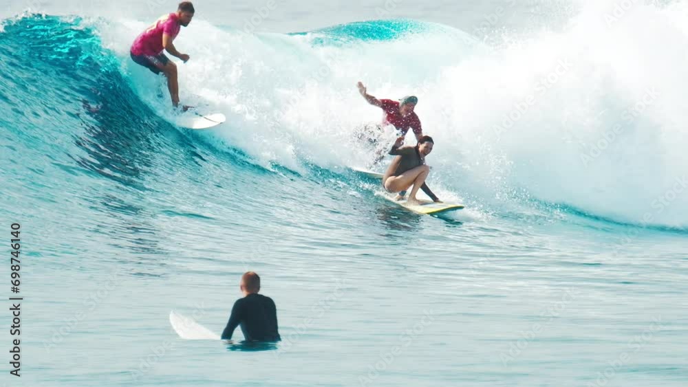 Woman surfer rides the wave in the ocean with men surfers dropping her ...
