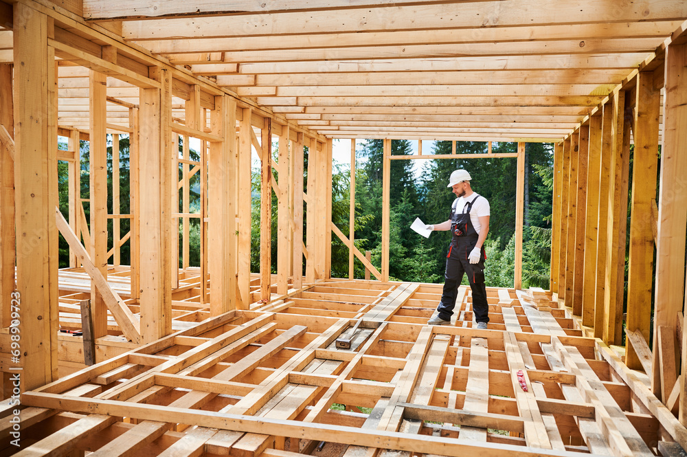 Worker building wooden two-story house near the forest. Man in work ...