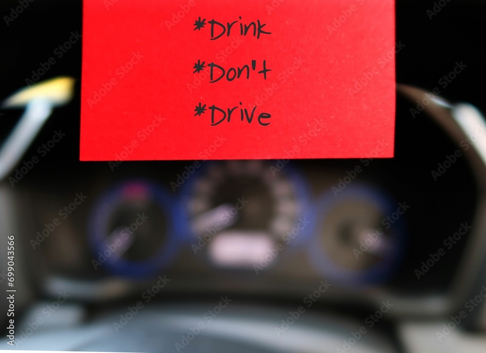Red stick note with text written DRINK DON'T DRIVE on the car steering ...