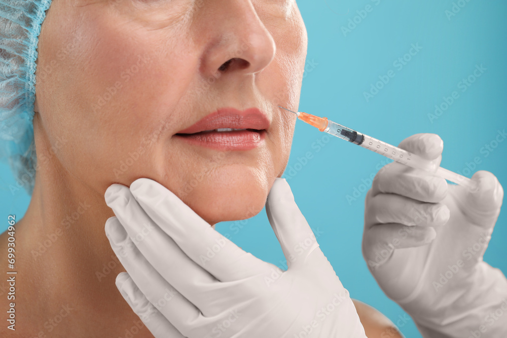 Doctor giving facial injection to senior woman on light blue background ...