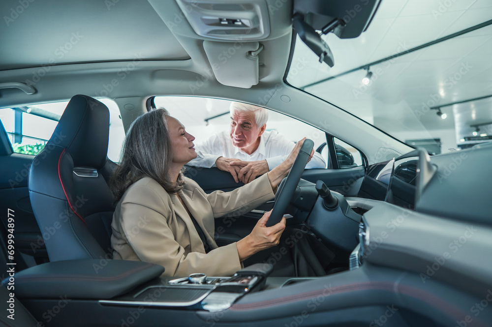 An elderly couple chooses a new car at a car dealership. Mature woman ...