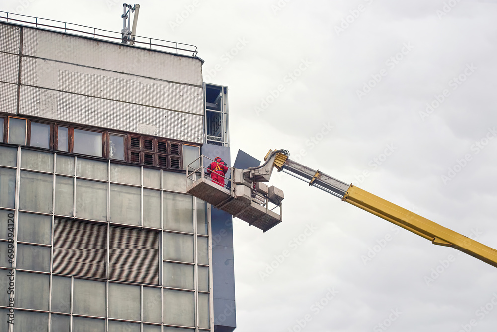 Workers in boom lift repair and install LED billboard on building. Man ...