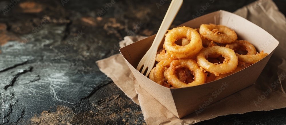 Battered onion rings takeaway in a cardboard tray with a wooden fork ...