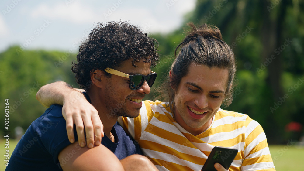 An LGBTQ male couple have a romantic moment using smarphone at the park ...