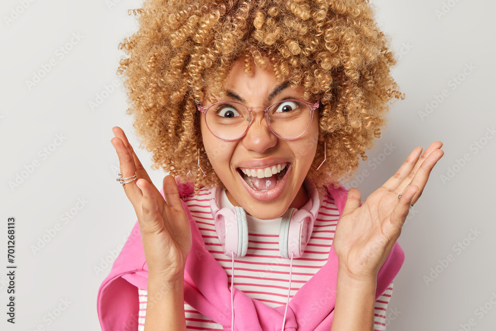 Crazy emotional angry woman with curly hair exclaims loudly keeps hands ...