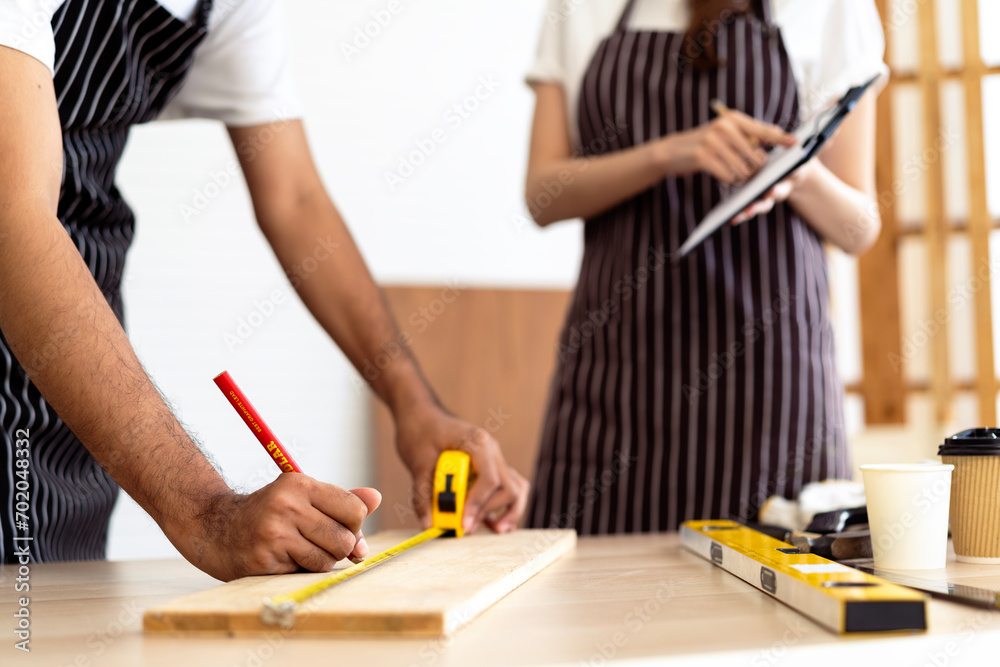 Skilled carpenters measuring wood boards with tape measure in organized ...