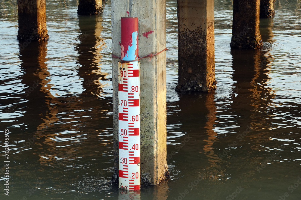Critical water level gauge. A red staff gauge beside a concrete pole ...