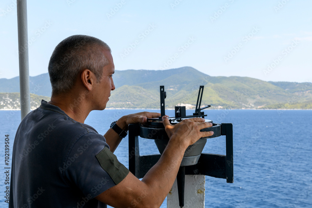Navigational officer taking bearing with azimuth ring on gyro compass ...