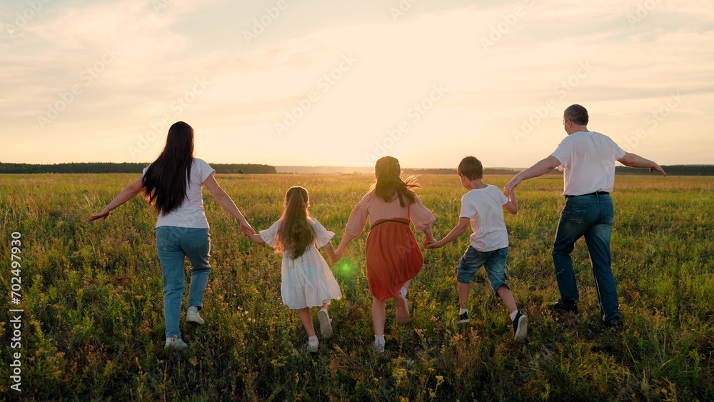 Parents, children run hand in hand across field at sunset. Family ...