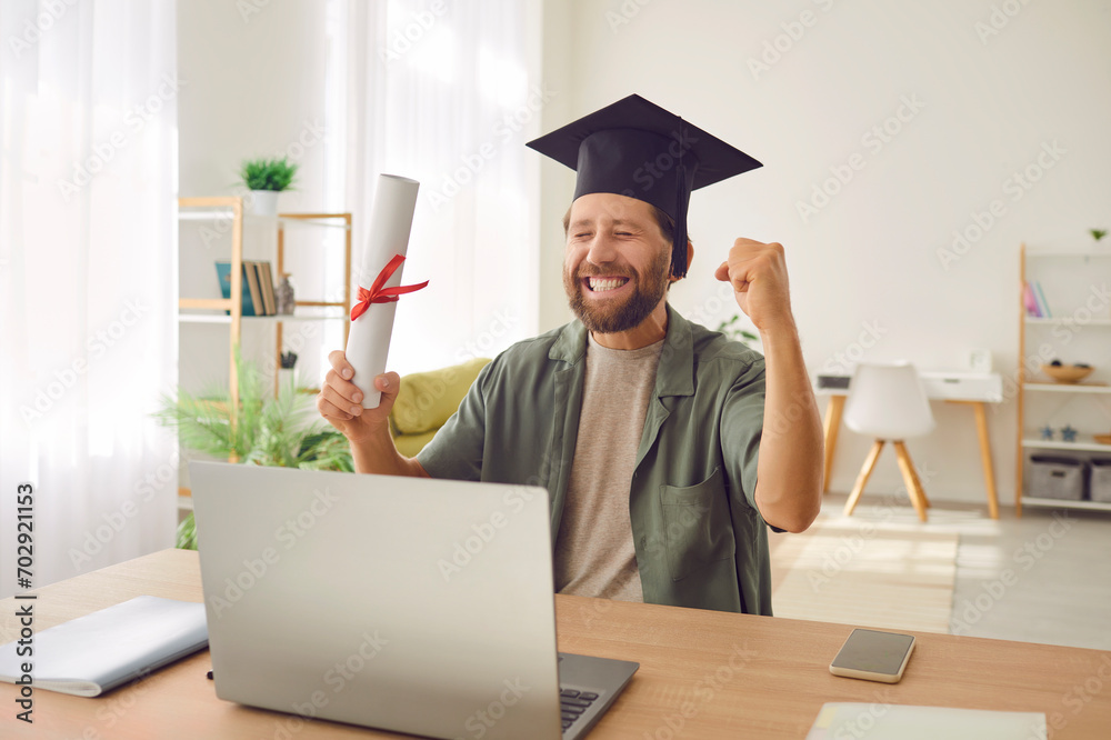 Happy excited graduate student man in hat sitting at the desk with ...