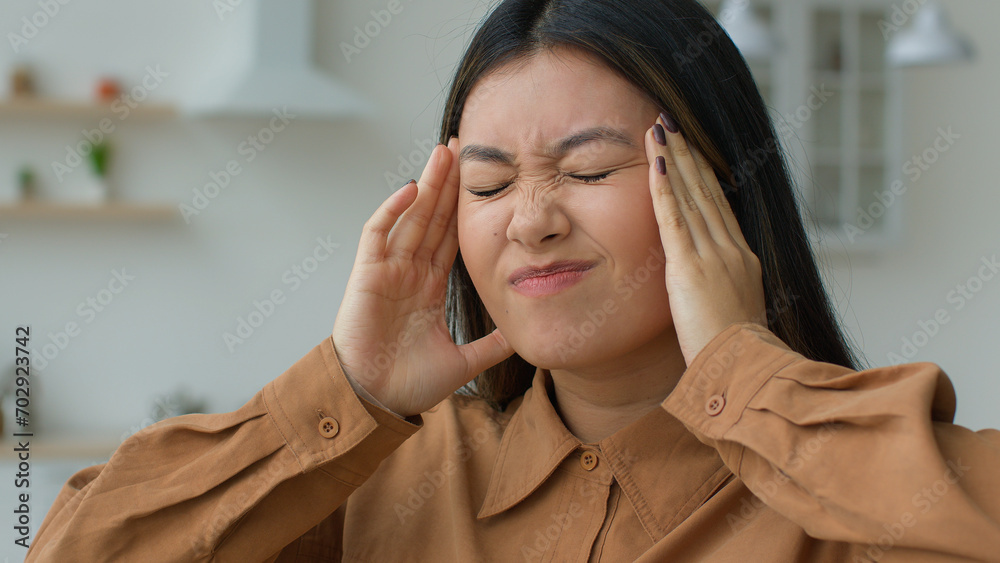 Tired sick Asian woman feel headache pain massaging temples touch aching head hurt grimace ...