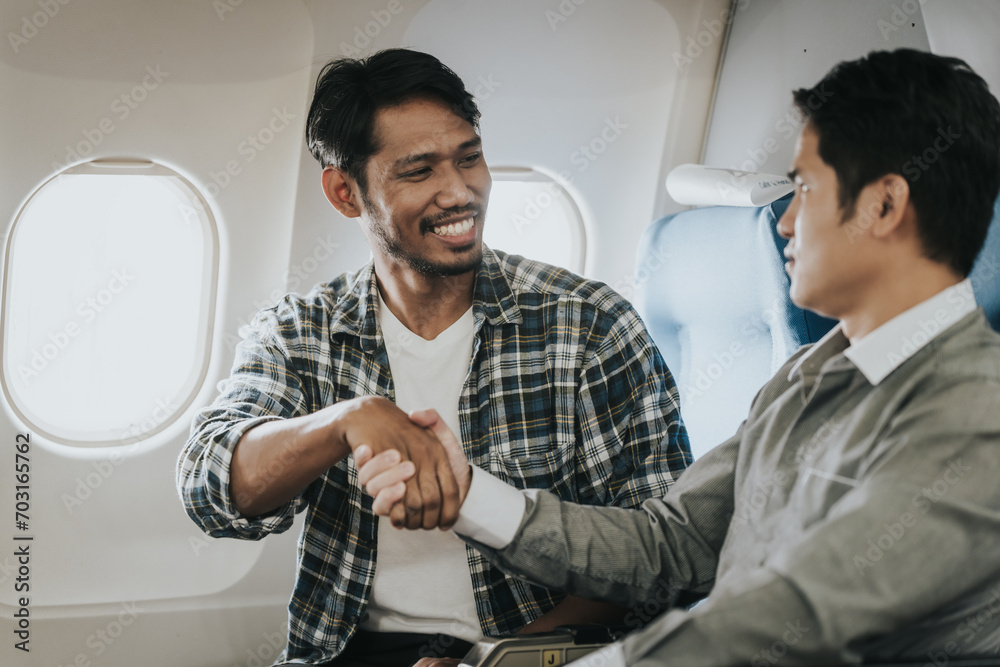 Shaking hands, two Asian men on an airplane, looking at a tablet ...