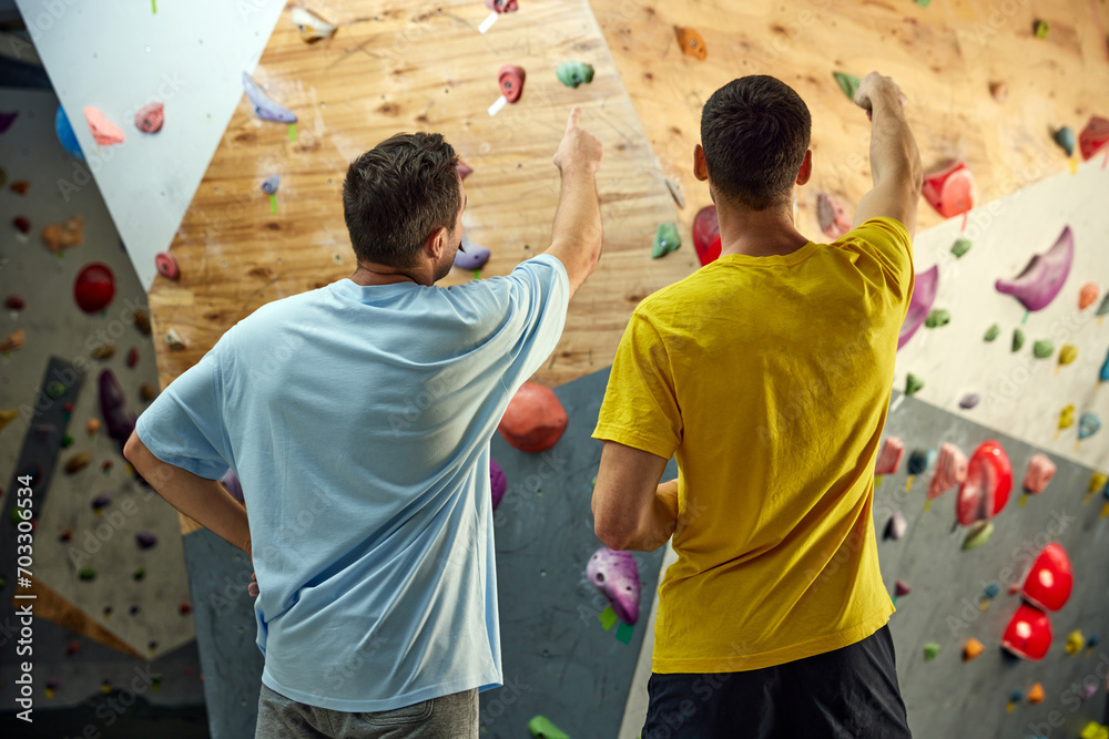 Man standing with instructor, looking and pointing on climbing wall ...