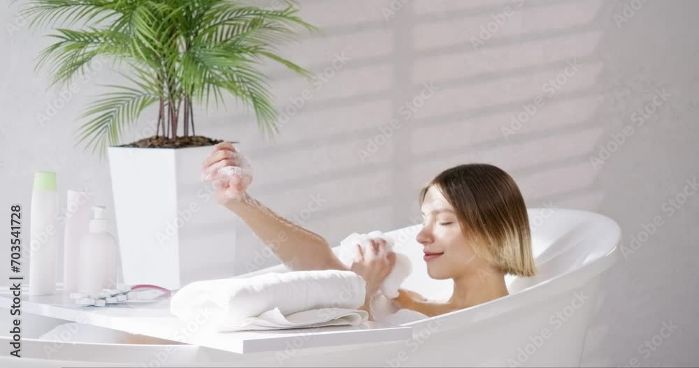 Calm fair-haired young female washing arms and body in warm bath in ...