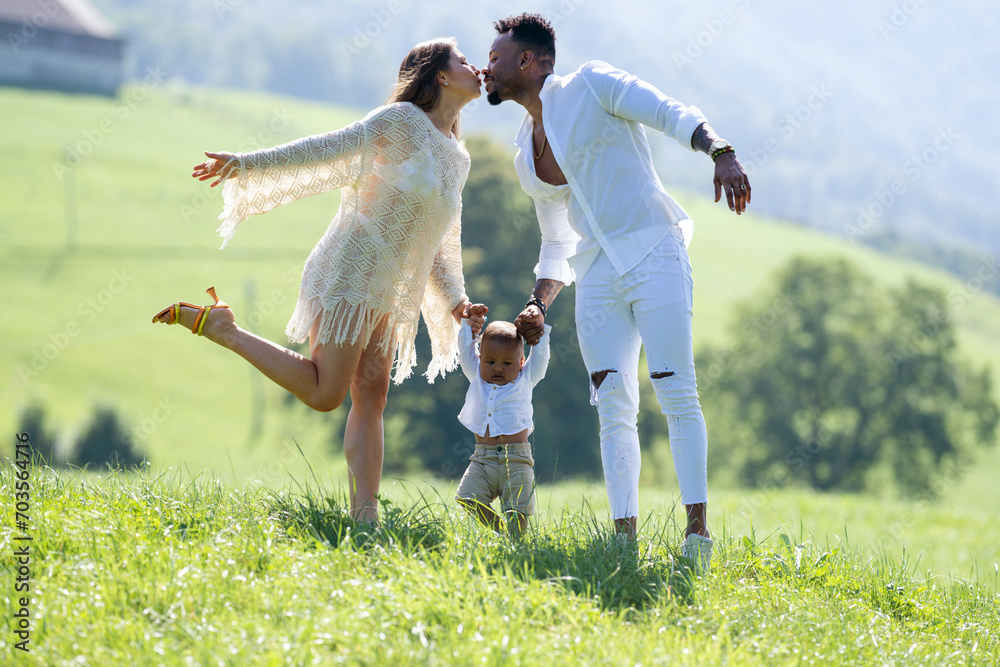 Multiethnic parents and mixed race baby walking on summer grass ...