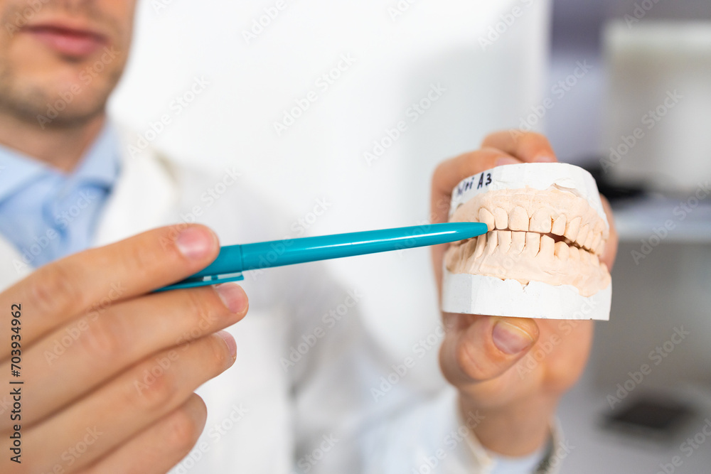Dental technician looking at plaster cast of jaws while making denture ...