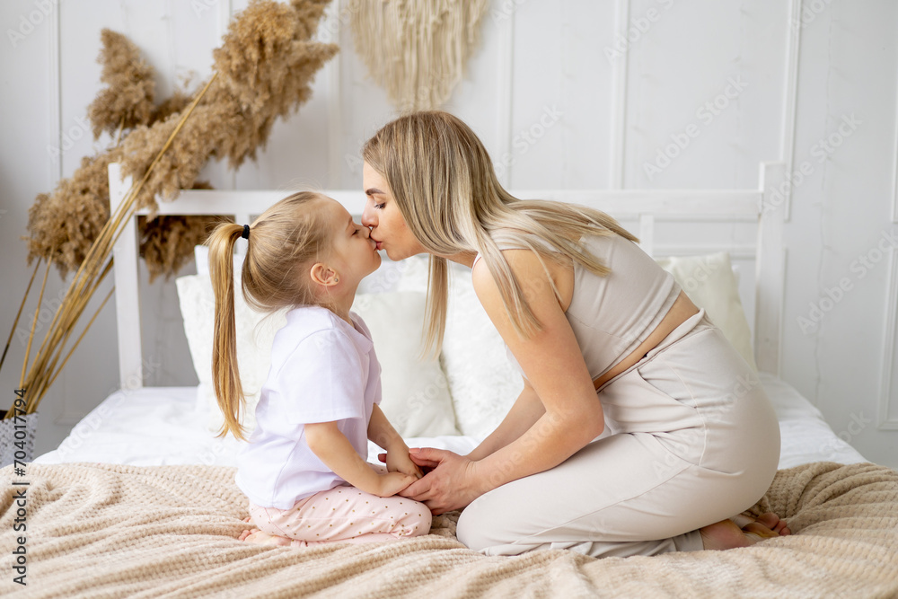 mom and daughter play, hug and kiss at home on the bed, lifestyle ...