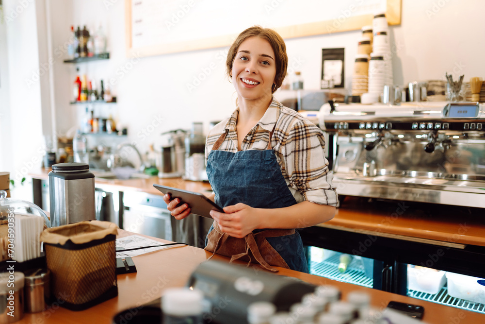 Portrait of a smiling cafe owner using a digital tablet behind the bar ...