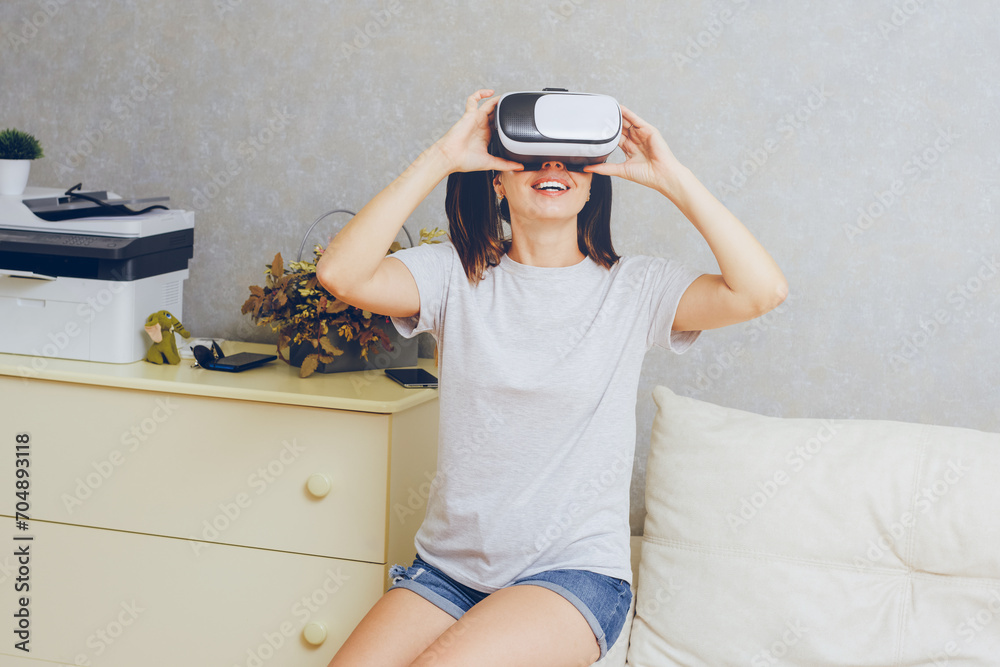 Captured in a cozy home setting, a young woman is immersed in a virtual reality experience ...