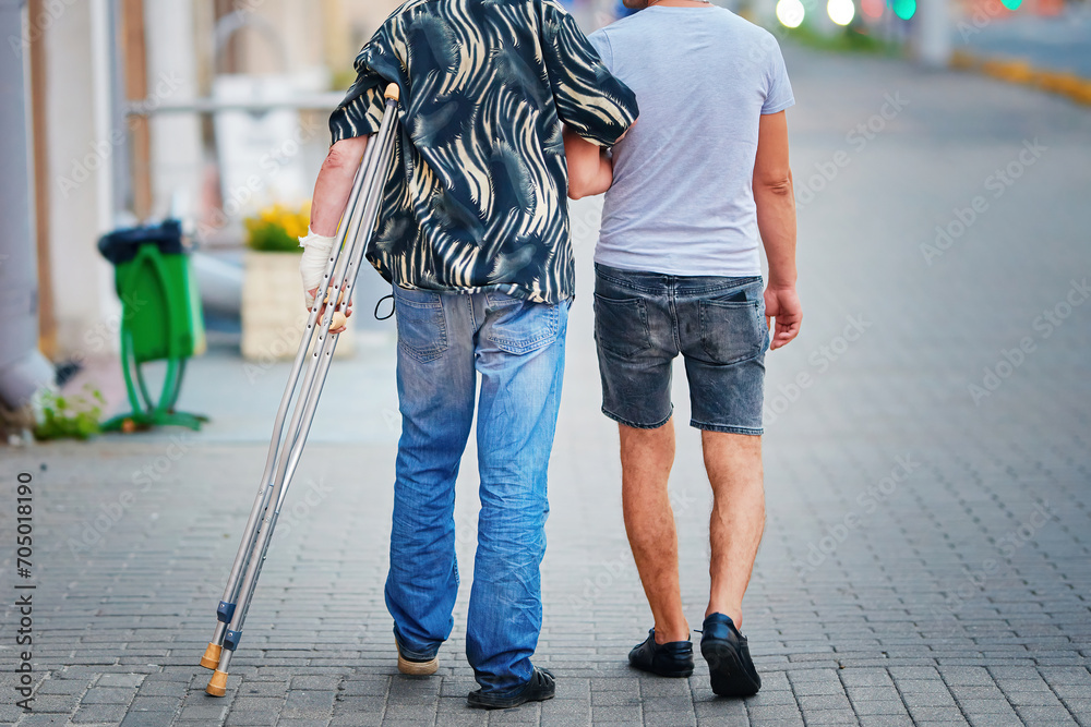 Mature man with bone fracture walking on city street with the help of ...