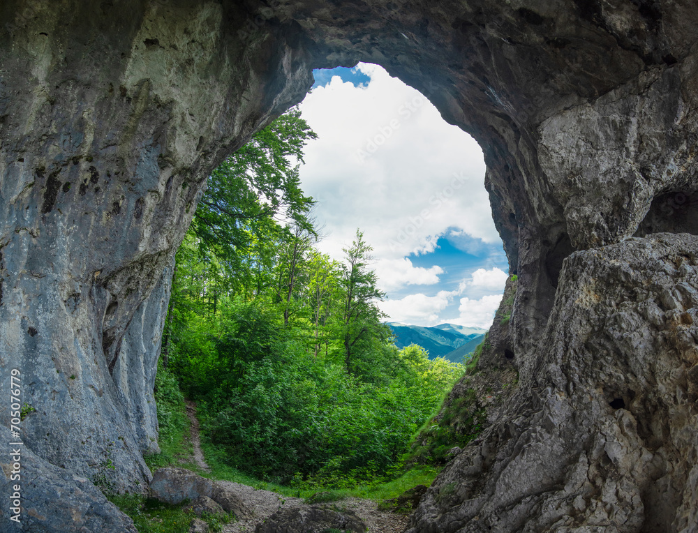 Viewpoint above a deciduous forest and mountains through a grotto ...