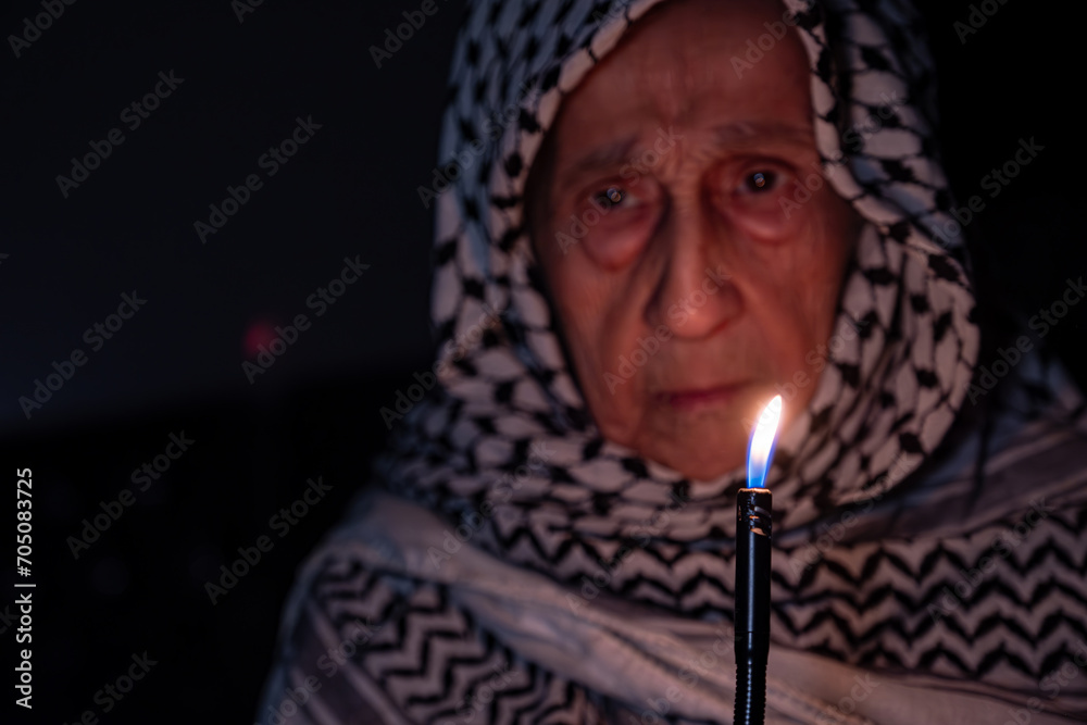 Portrait of old lady wearing white palestinian keffiyeh in dark holding ...