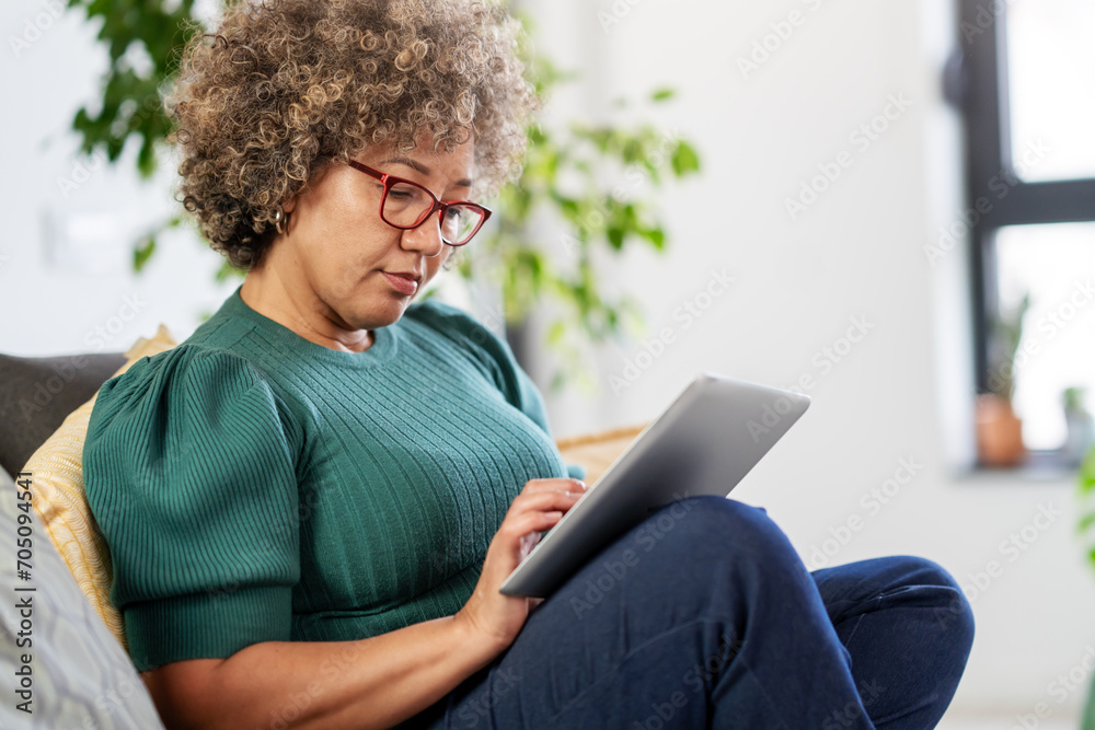 Beautiful middle-aged woman using a computer tablet to read a book and ...