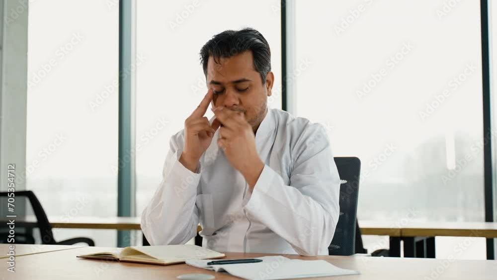 Stressed frustrated Indian doctor with headache sitting alone at work ...