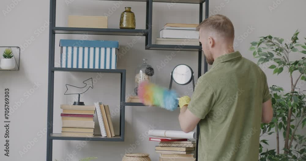 Diligent guy dusting furniture doing house chores using colorful duster ...