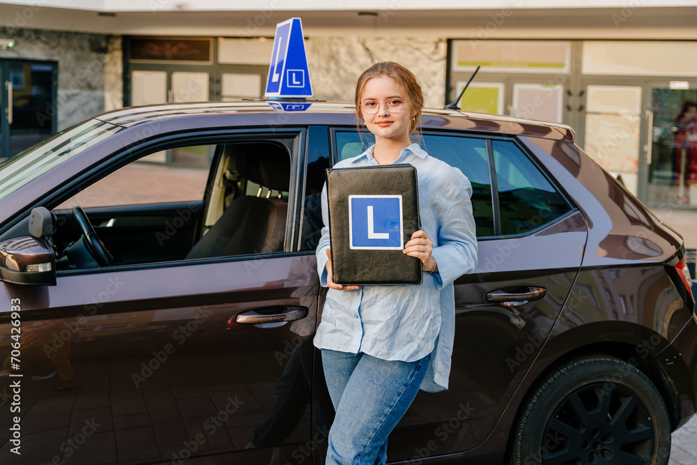 Young female learner driver hold clipboard with L sign standing next to ...