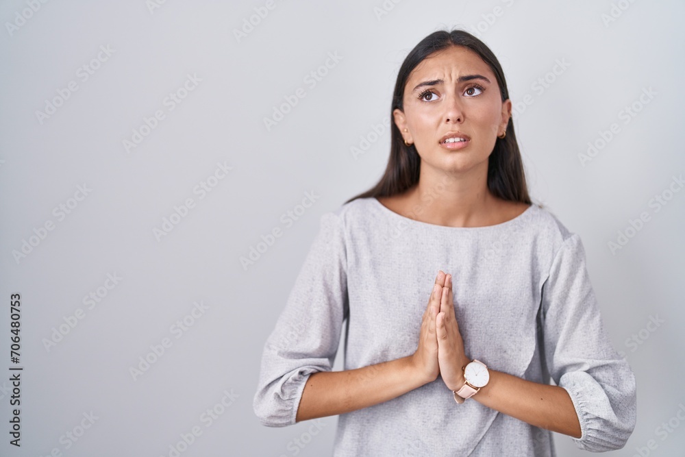 Young hispanic woman standing over white background begging and praying ...