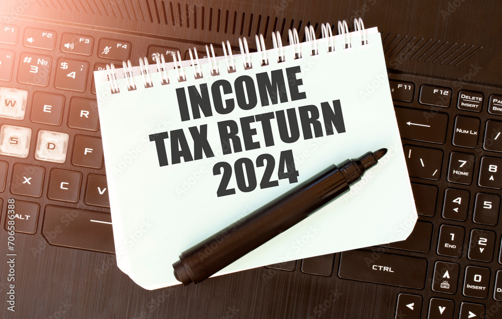 White paper sheet with text INCOME TAX RETURN 2024 on the black laptop ...