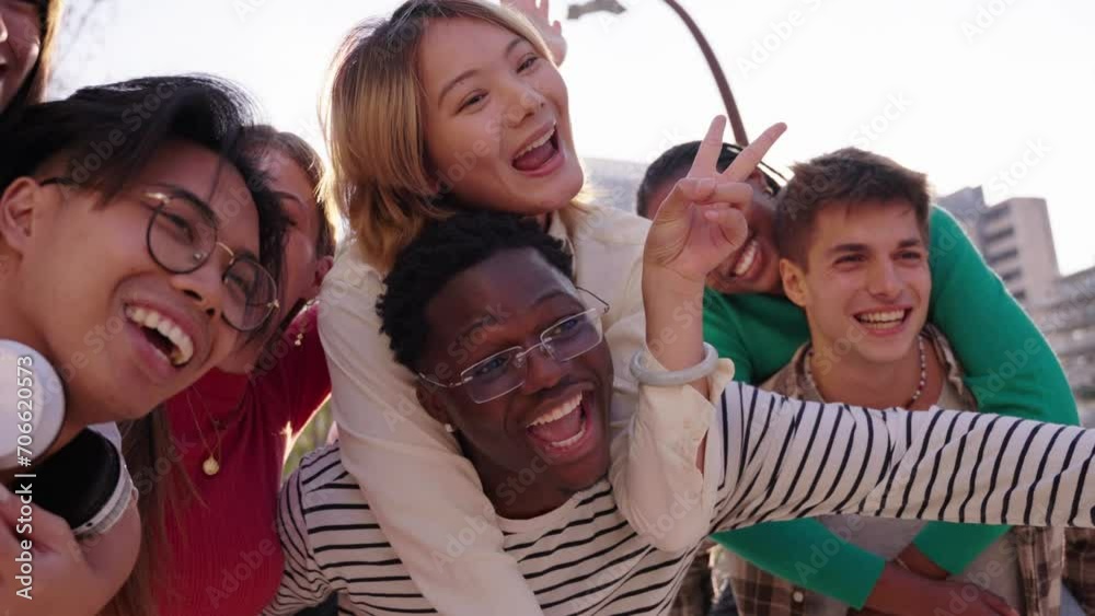 A large group of smiling and cheerful young multiracial university students taking a selfie with ...