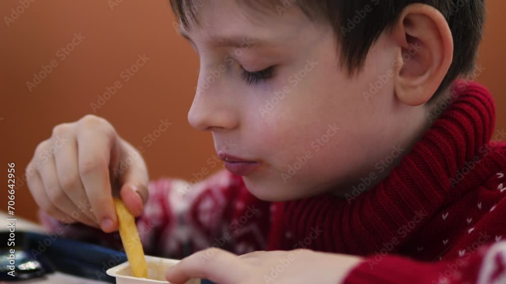 portrait of a Caucasian boy eating French fries dipping them into sauce ...