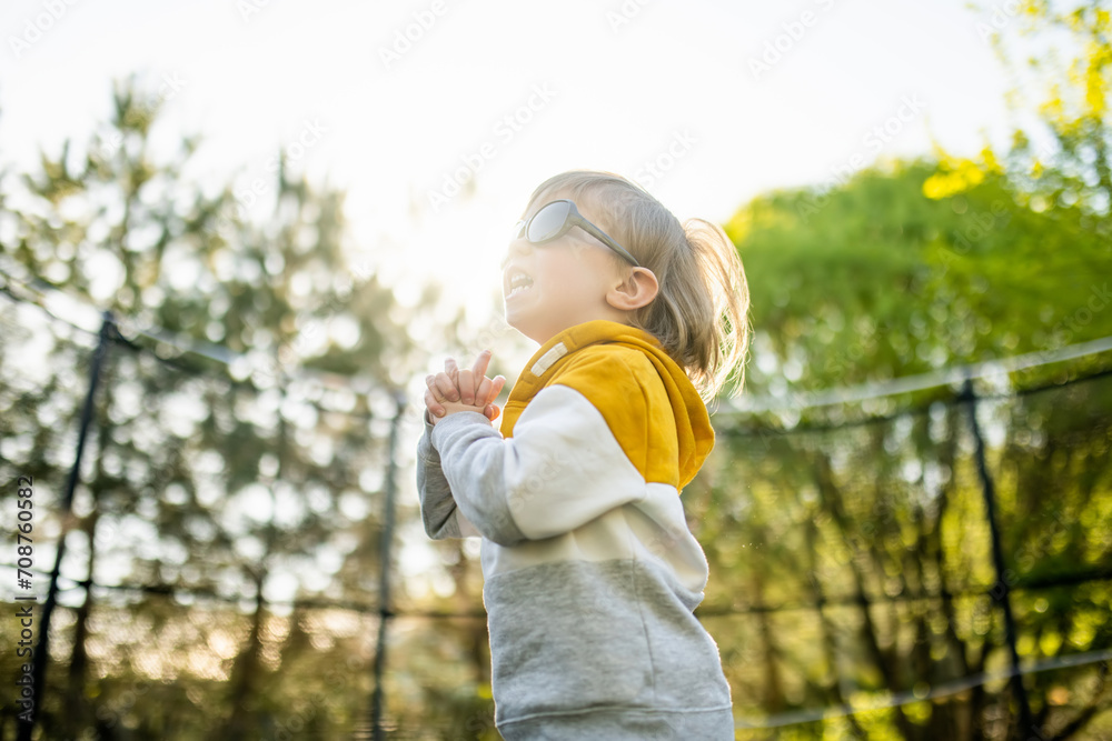 Cute little boy jumping on a trampoline in a backyard on warm and sunny ...