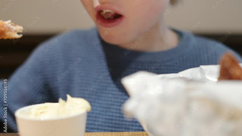 Cute blonde preteen boy eating chicken nuggets or wings with sauce at ...