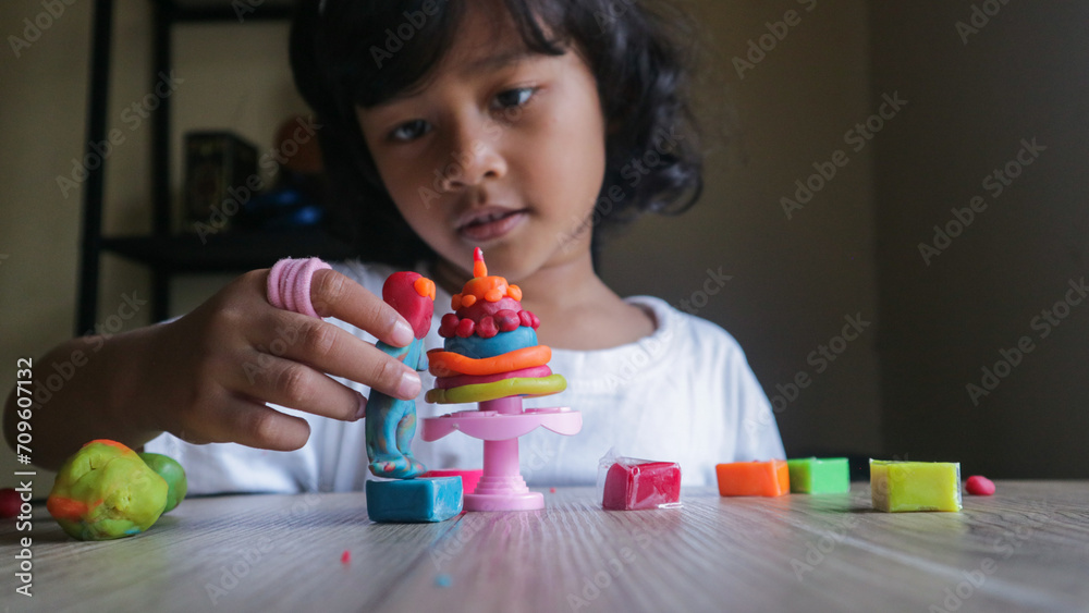 Little girl child sitting at table playing with play doh or plasticine ...