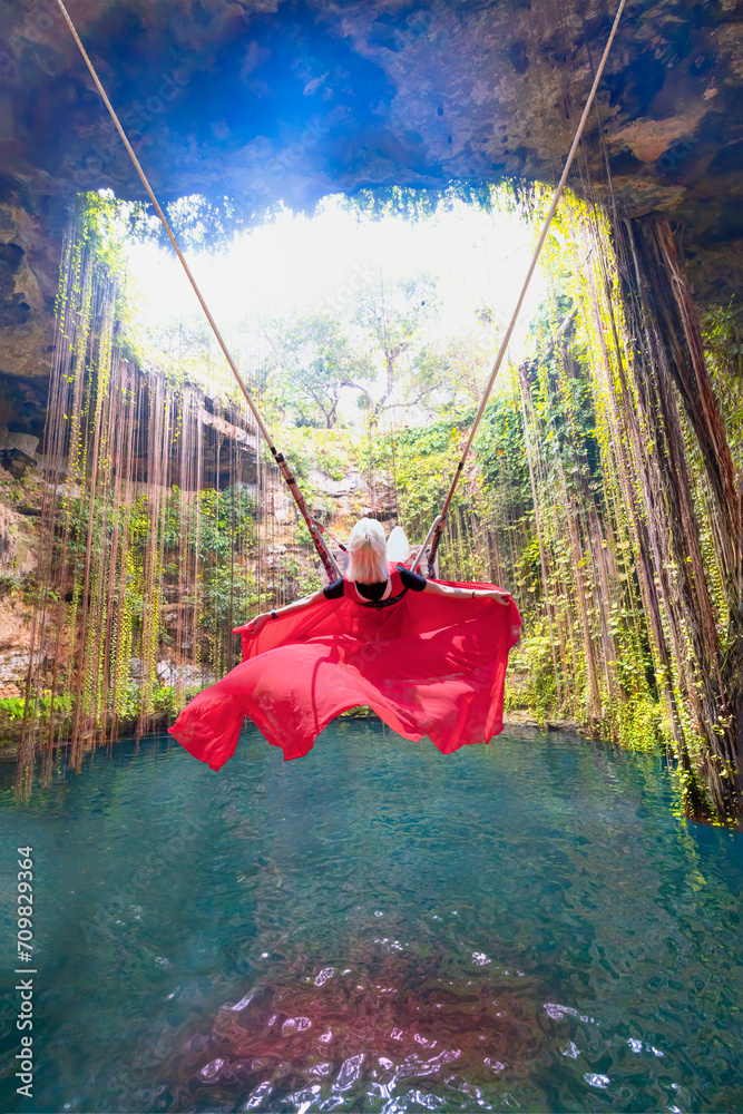 A beautiful young blonde girl wearing a long red dress swings on a ...