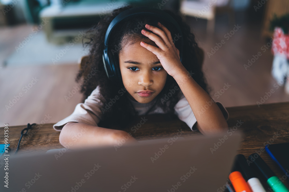 Pensive African-American girl with headphones looking at a laptop ...