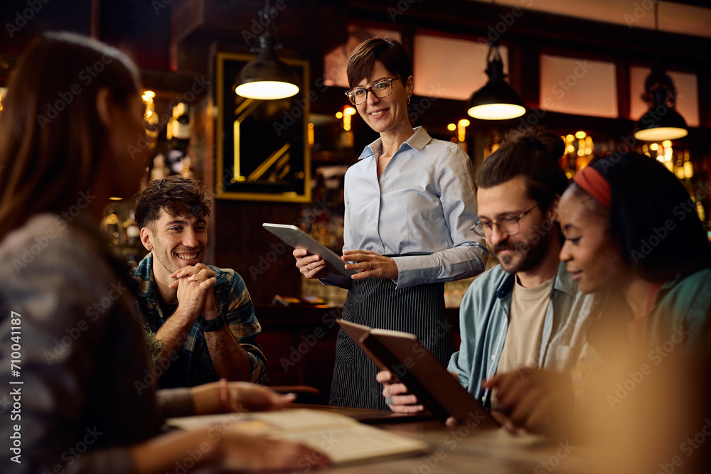 Happy waitress using touchpad while talking to guests in bar. Stock ...