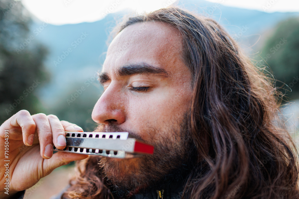 a young man with long hair plays the harmonica. a man enjoys playing ...