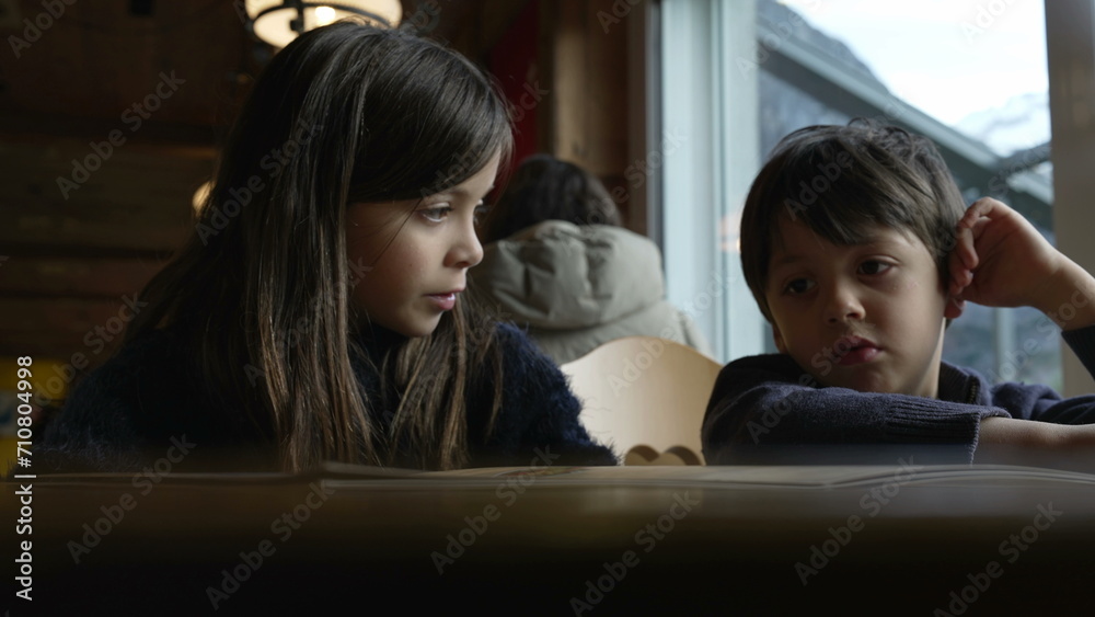 Young siblings looking at restaurant menu, sister assisting younger ...