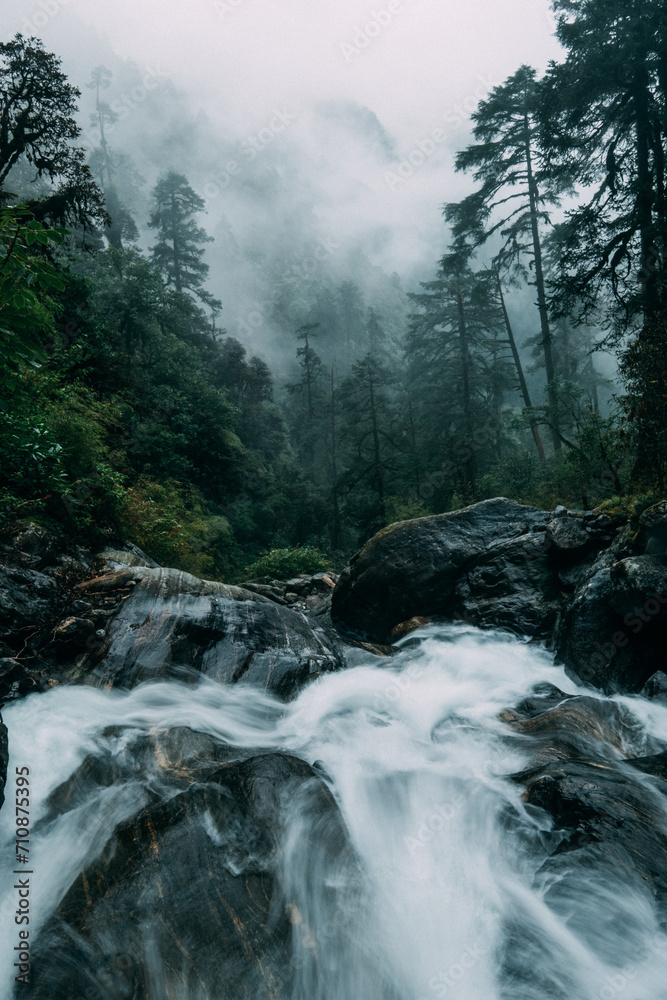 Powerful mountain creek running through the big boulders down the foggy ...