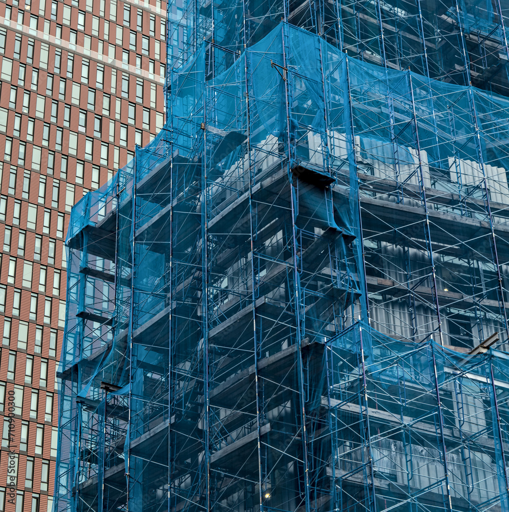 building under construction covered in blue mesh tarp protective wrap ...