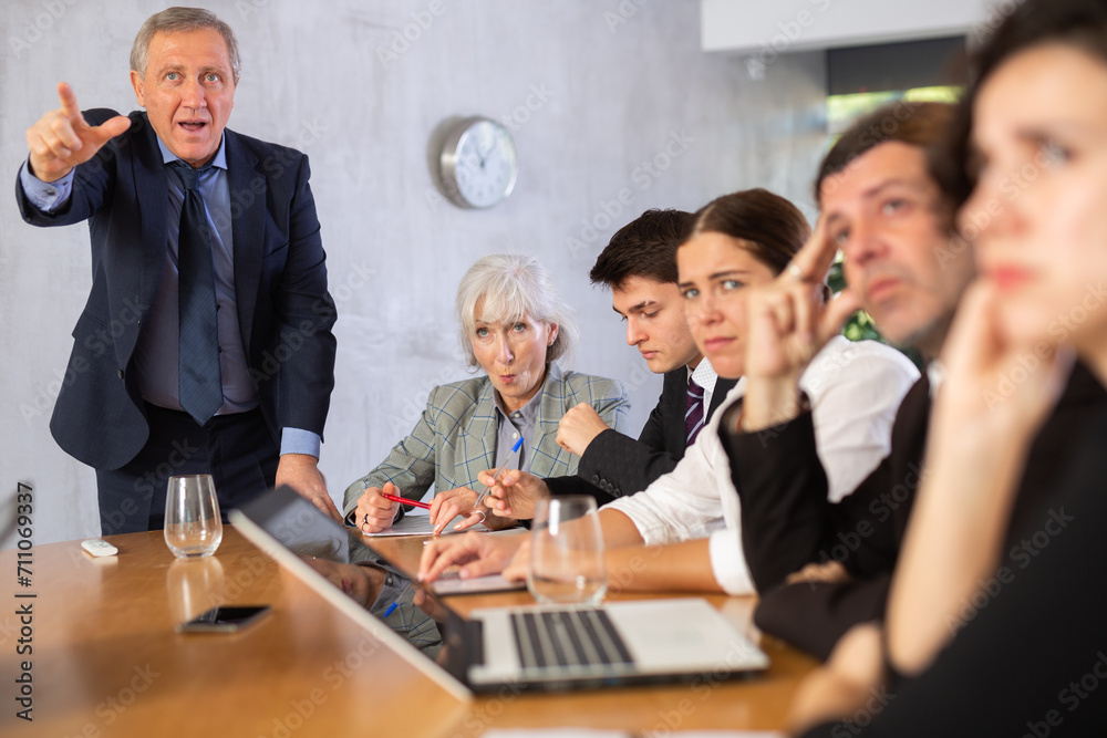 Angry elderly male boss scolding office workers of different ages using ...