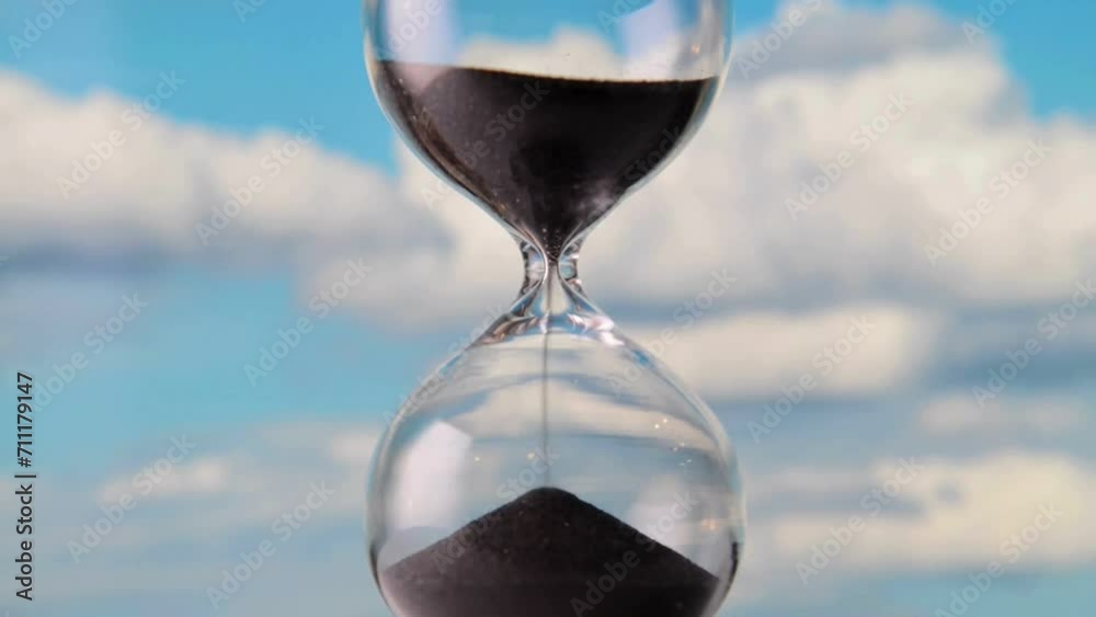 hourglass with clouds rolling in the background. The sand in the clock ...