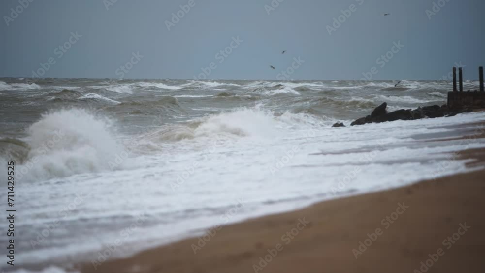 Choppy waves crash on sandy shore under overcast sky. Storm surge hits ...