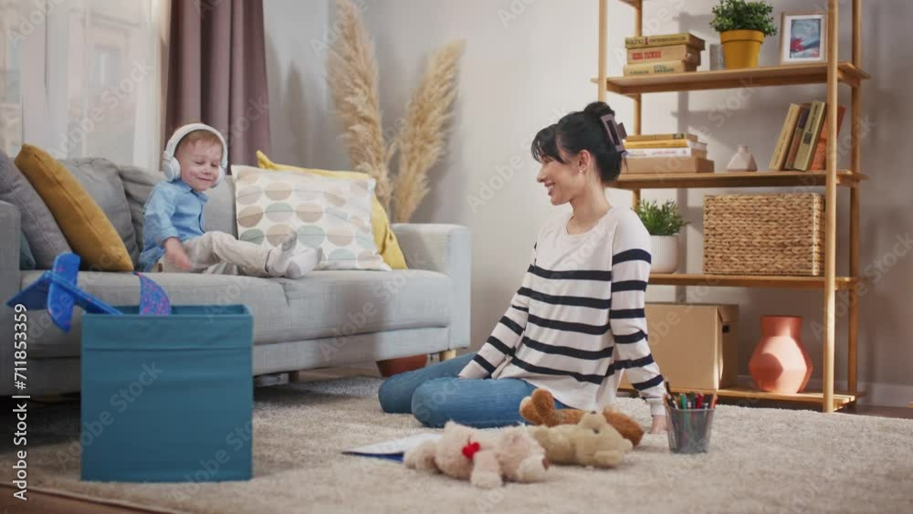 Cheerful mother enjoying rising little son. Kiddo wearing headphones ...