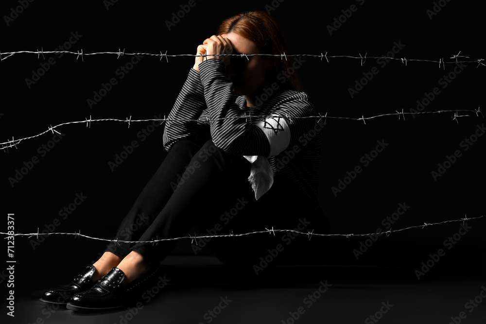 Mature Jewish woman sitting behind barbed wire on black background ...
